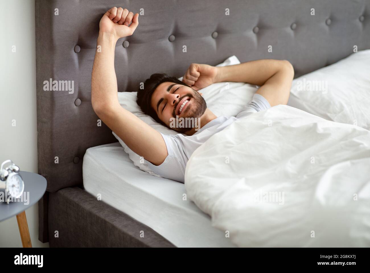 Rested arab man waking up and stretching hands, wellslept guy lying in ...