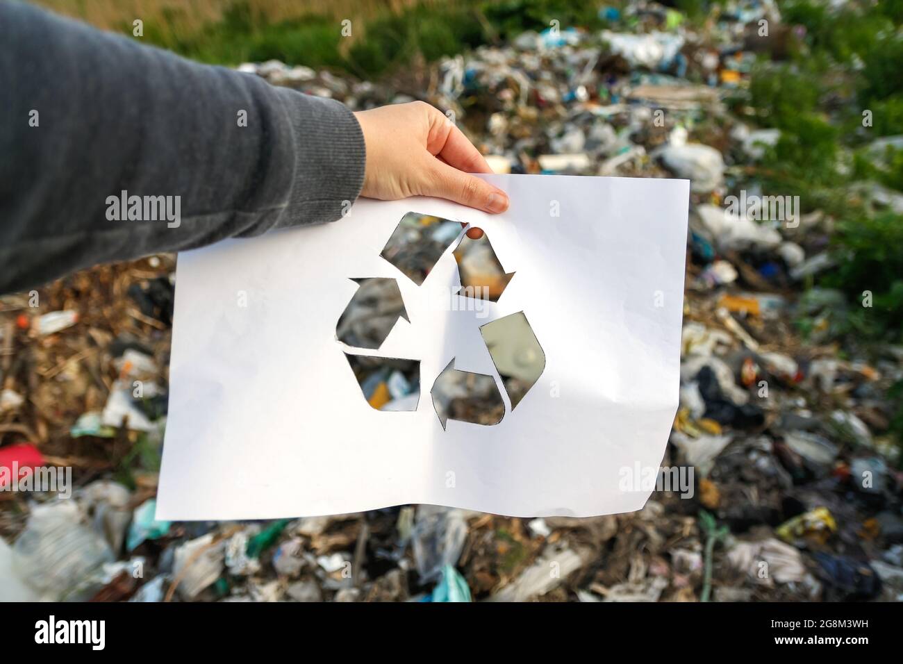 Hand holding cut paper with the logo of recycling on dump garbage trash ...