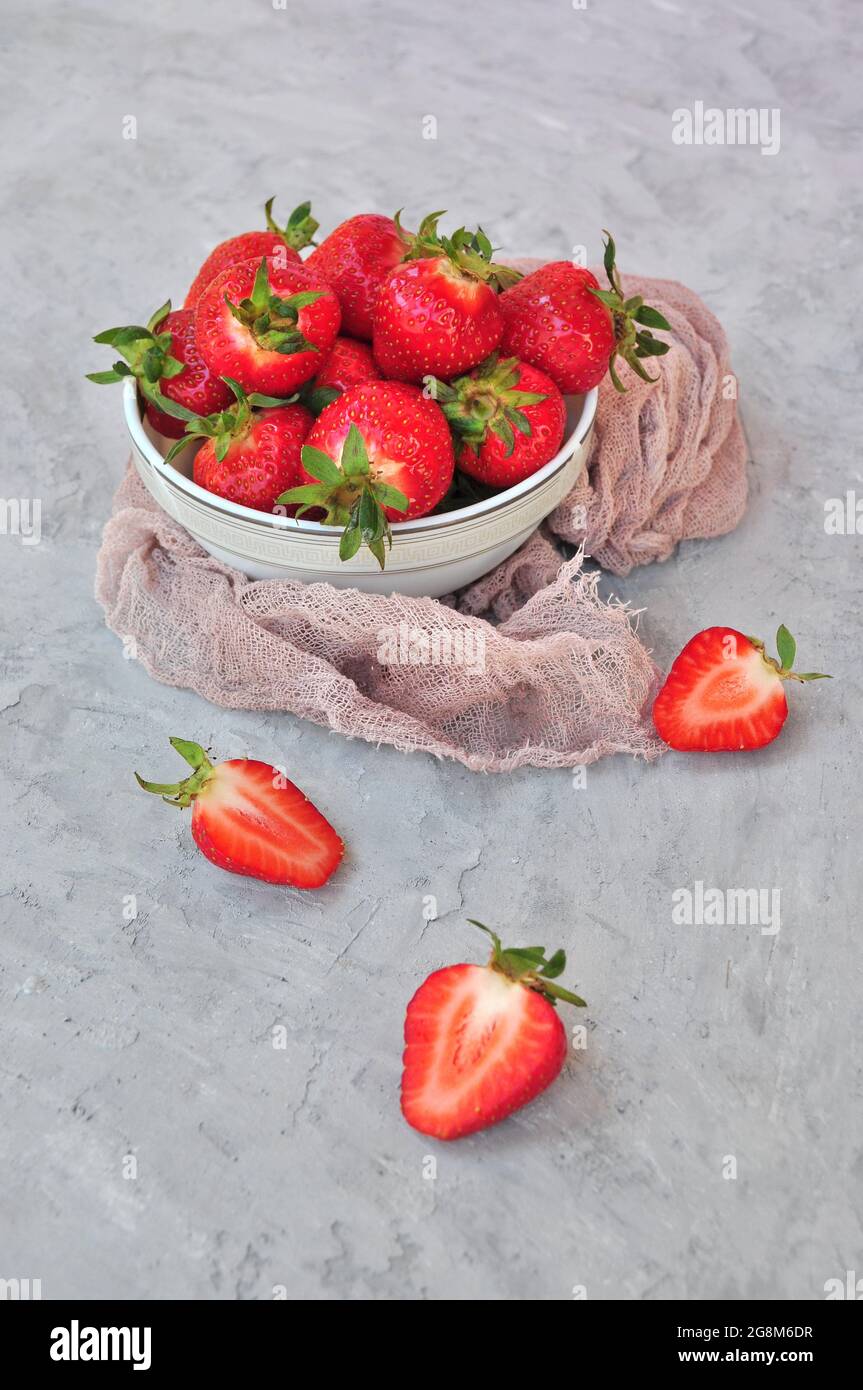 Fresh ripe sweet whole and cut strawberries in a pink bowl on a gray ...