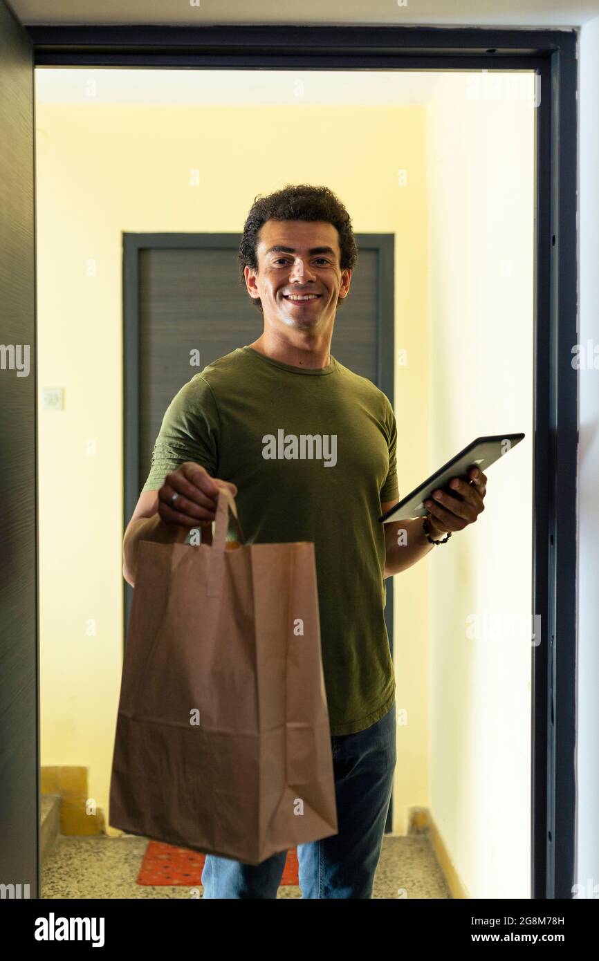 A smiling delivery man holds a tablet in his hand and hands out a paper ...