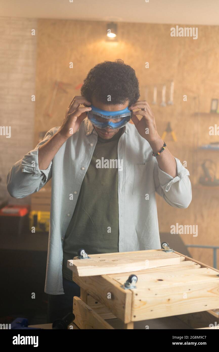 Portrait of a carpenter putting on safety goggles over his head in his ...
