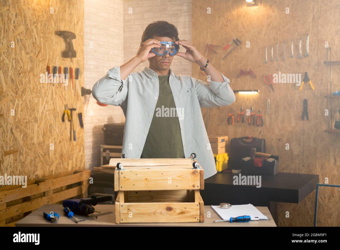 Portrait of a carpenter putting on safety goggles over his head in his ...