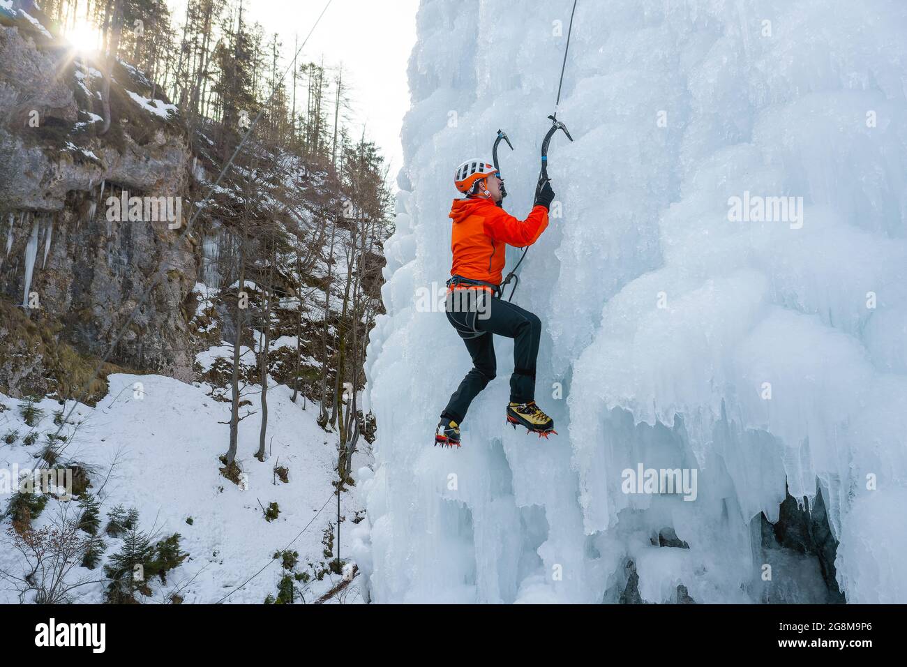Aerial shot of an ice climber ascending the ice waterfall in the sun ...
