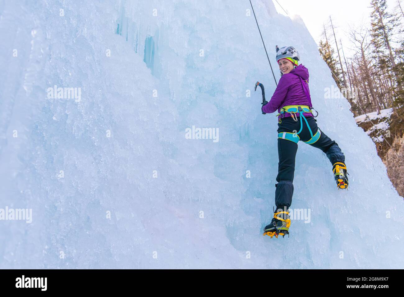 Female ice climber going down an ice waterfall, using a safety top rope ...