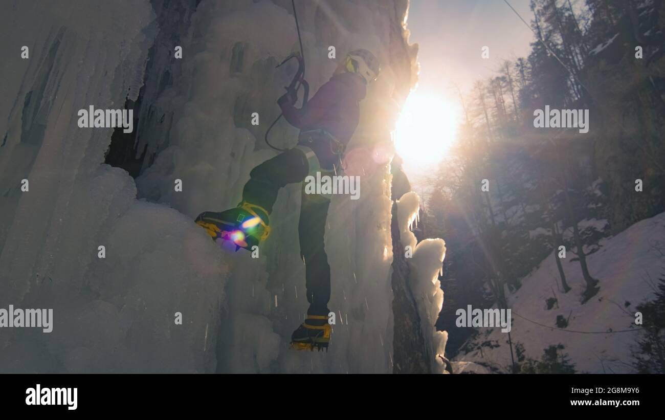 Female ice climber hiking on a vertical frozen ice surface, making ...