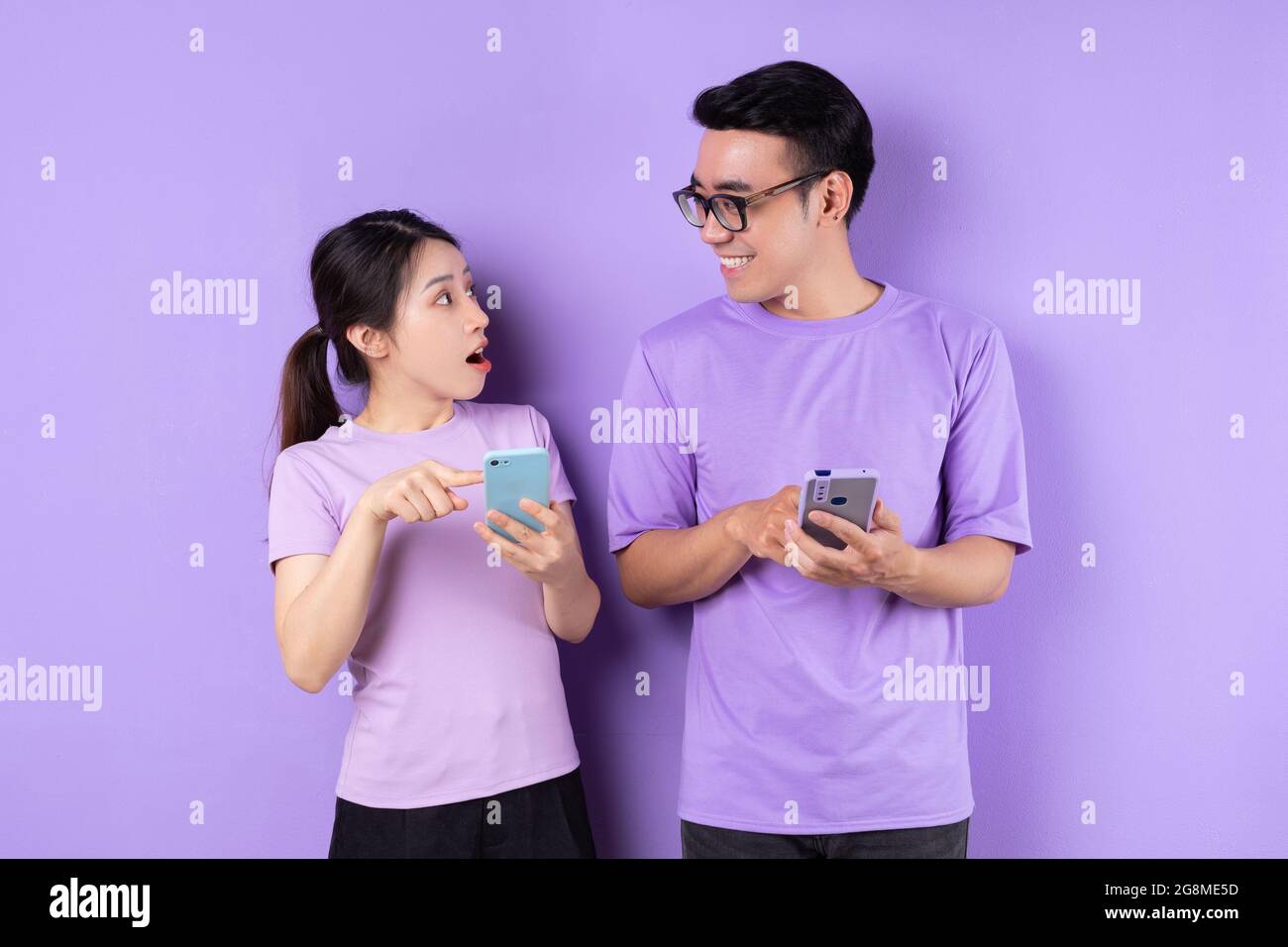 Young Vietnamese friends using their smartphone on purple background ...
