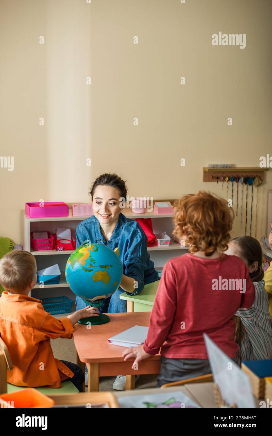 smiling teacher talking to kids near globe in classroom Stock Photo - Alamy