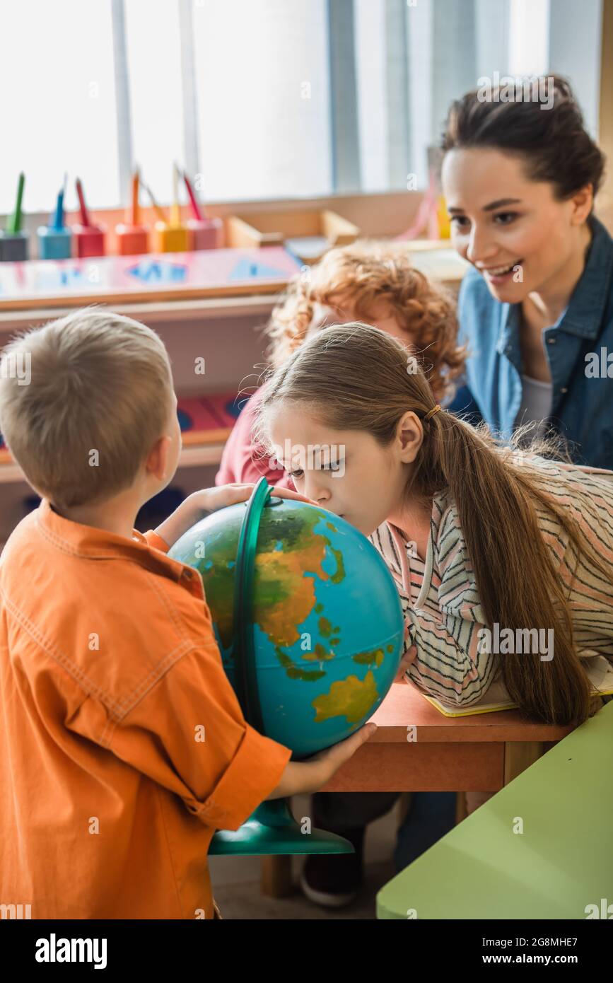 curious girl looking at globe near children and blurred teacher in ...