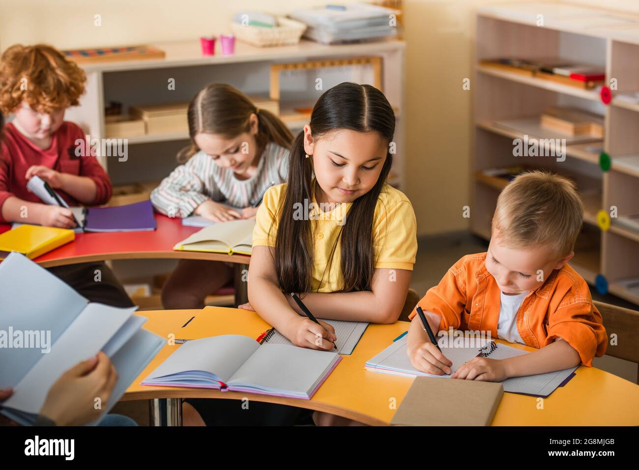 multiethnic kids writing in notebooks during lesson in montessori ...