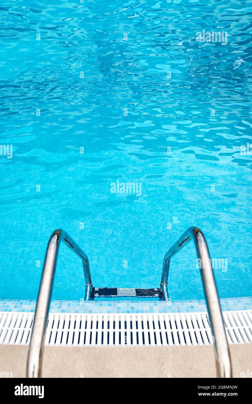 Top step and chrome hand rails of a swimming pool ladder and blue pool ...