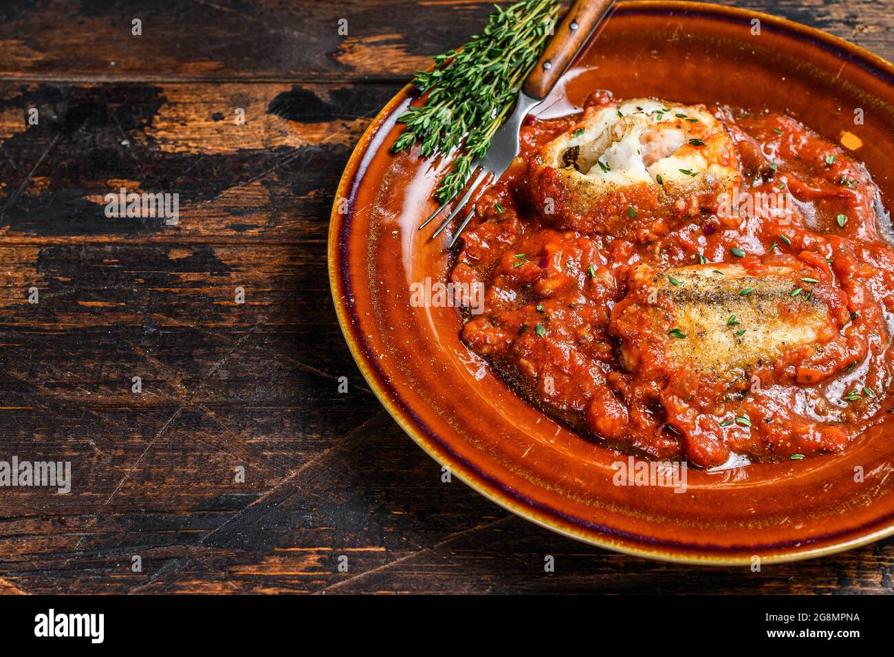 Roast grenadier white fish fillet with tomato sauce in a plate. Dark ...