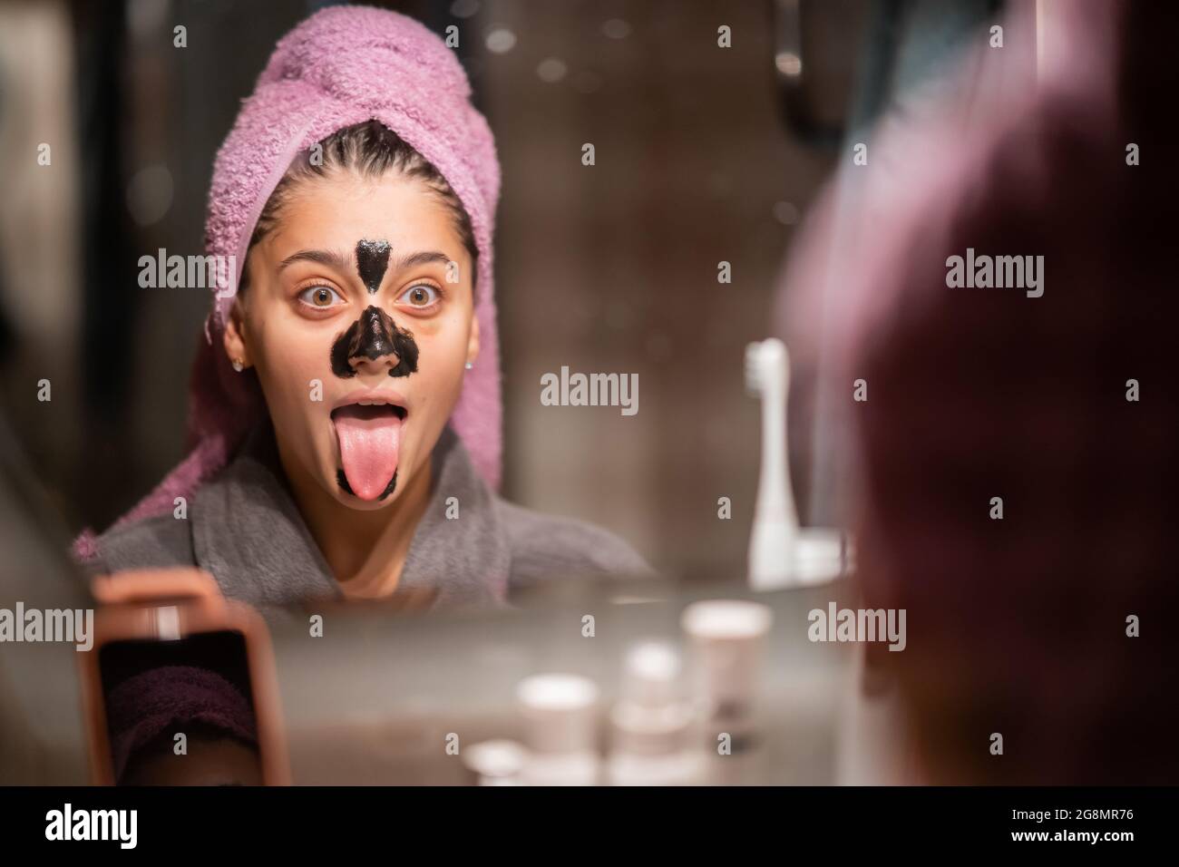 Beautiful woman with a clay or a mud mask on her face showing tongue ...