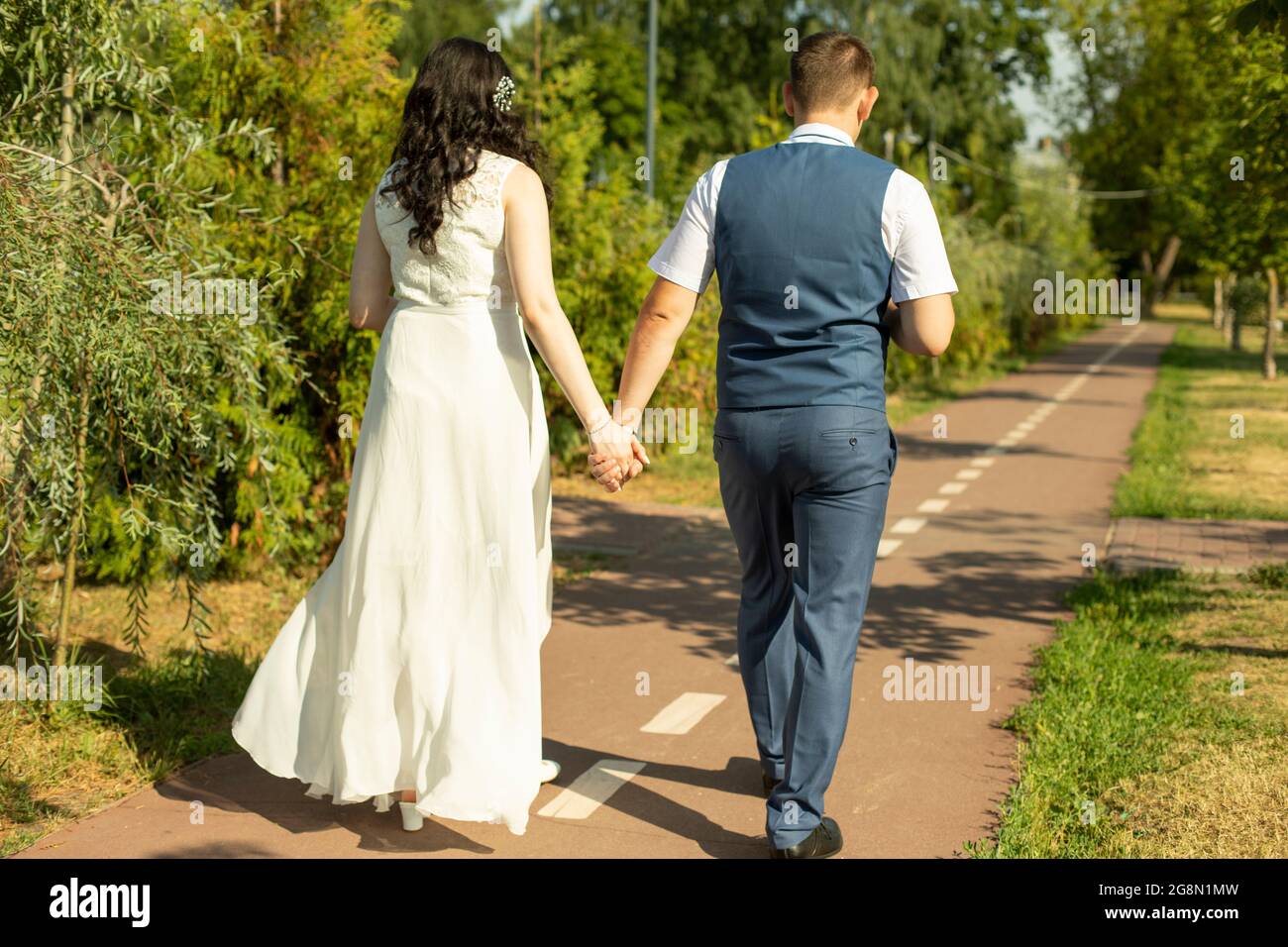 The newlyweds walk along the park path holding hands. A guy and a girl ...