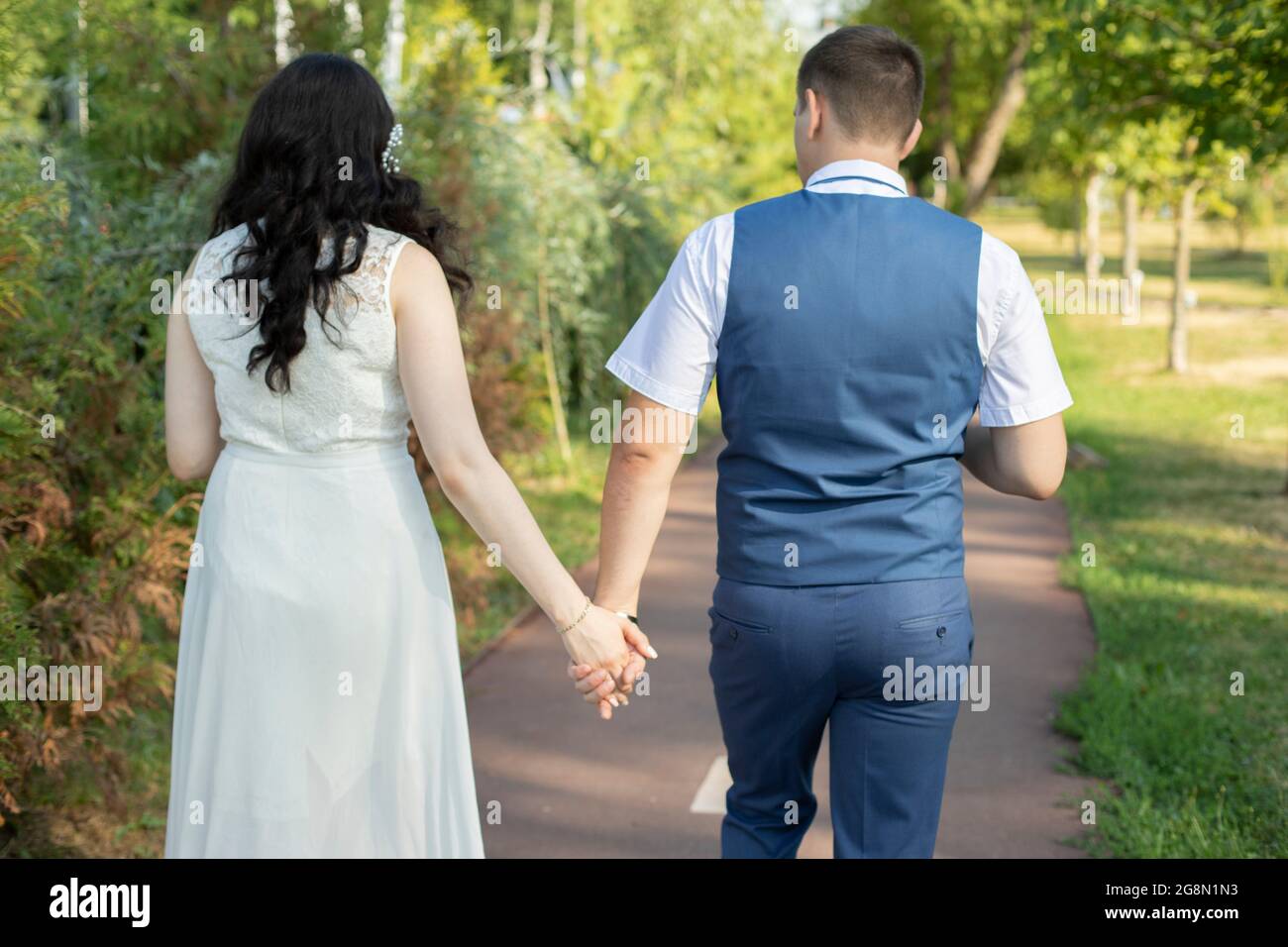 The newlyweds walk along the park path holding hands. A guy and a girl ...
