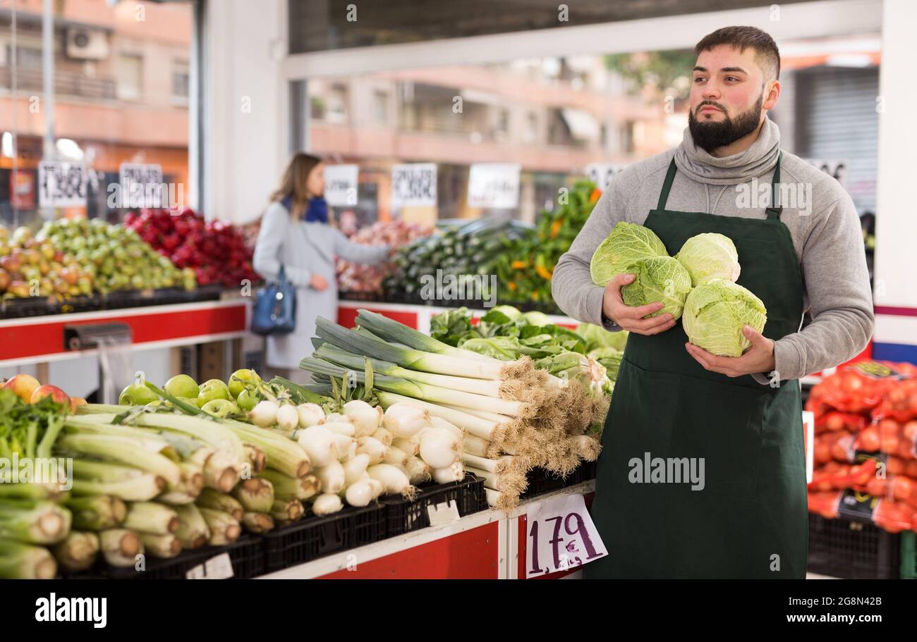 Male shop assistant lays fresh cabbage on counter in grocery shop Stock ...