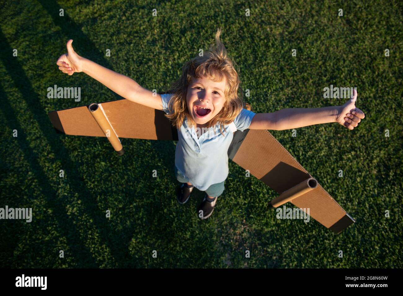 Excited funny child boy flying in plane made craft of cardboard wings ...