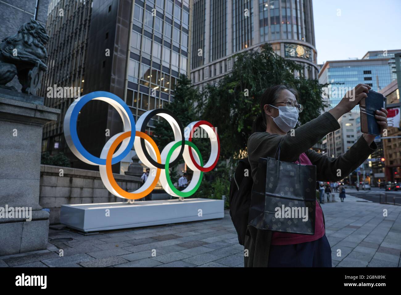 A woman wearing a mask takes a selfie in front of the Olympic Rings ...