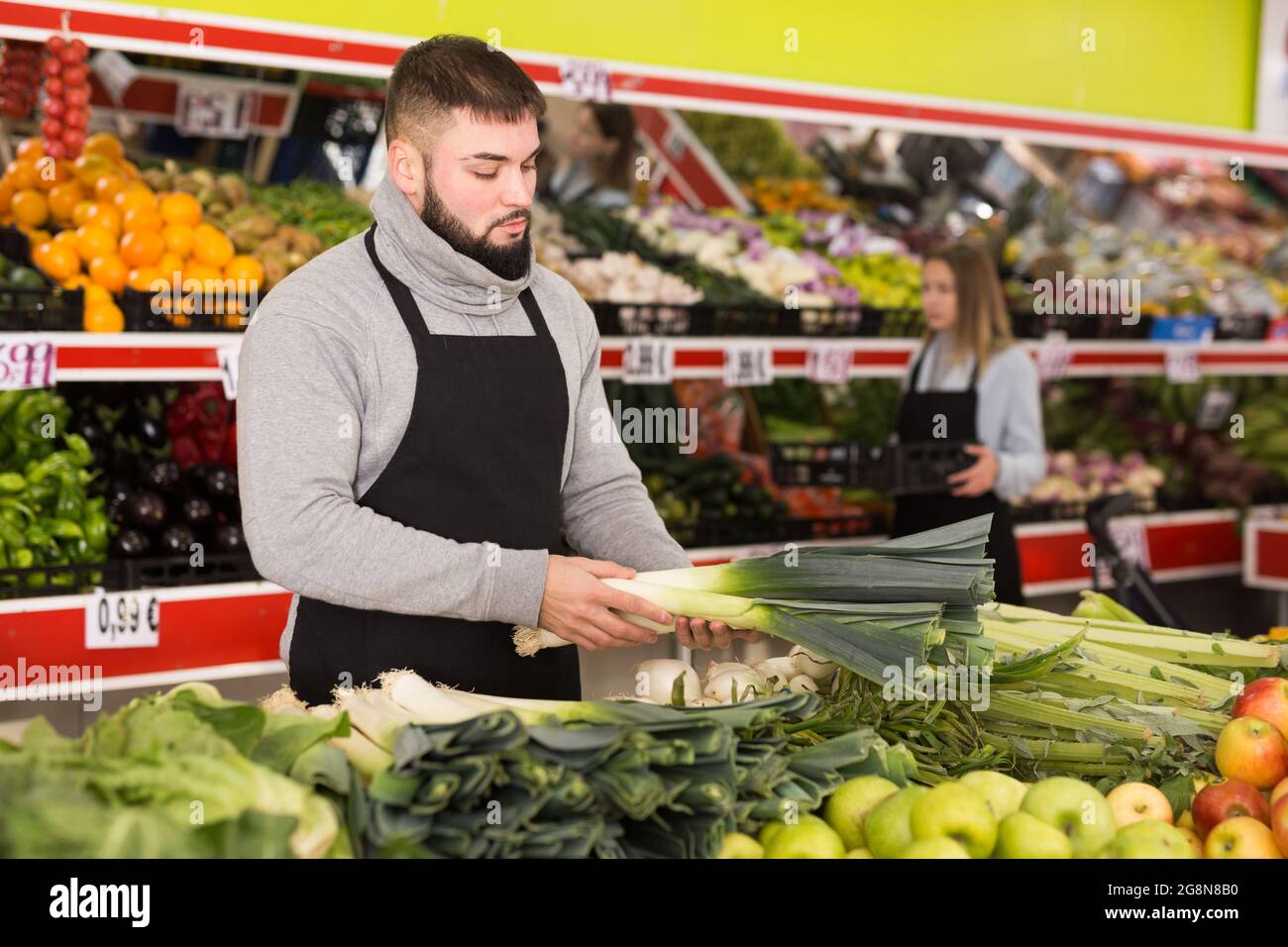 Male shop assistant lays fresh leek on counter in grocery shop Stock ...