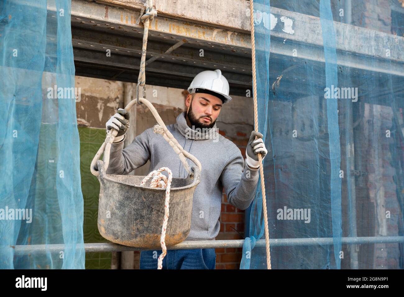 Guy lowering down bucket on rope Stock Photo - Alamy
