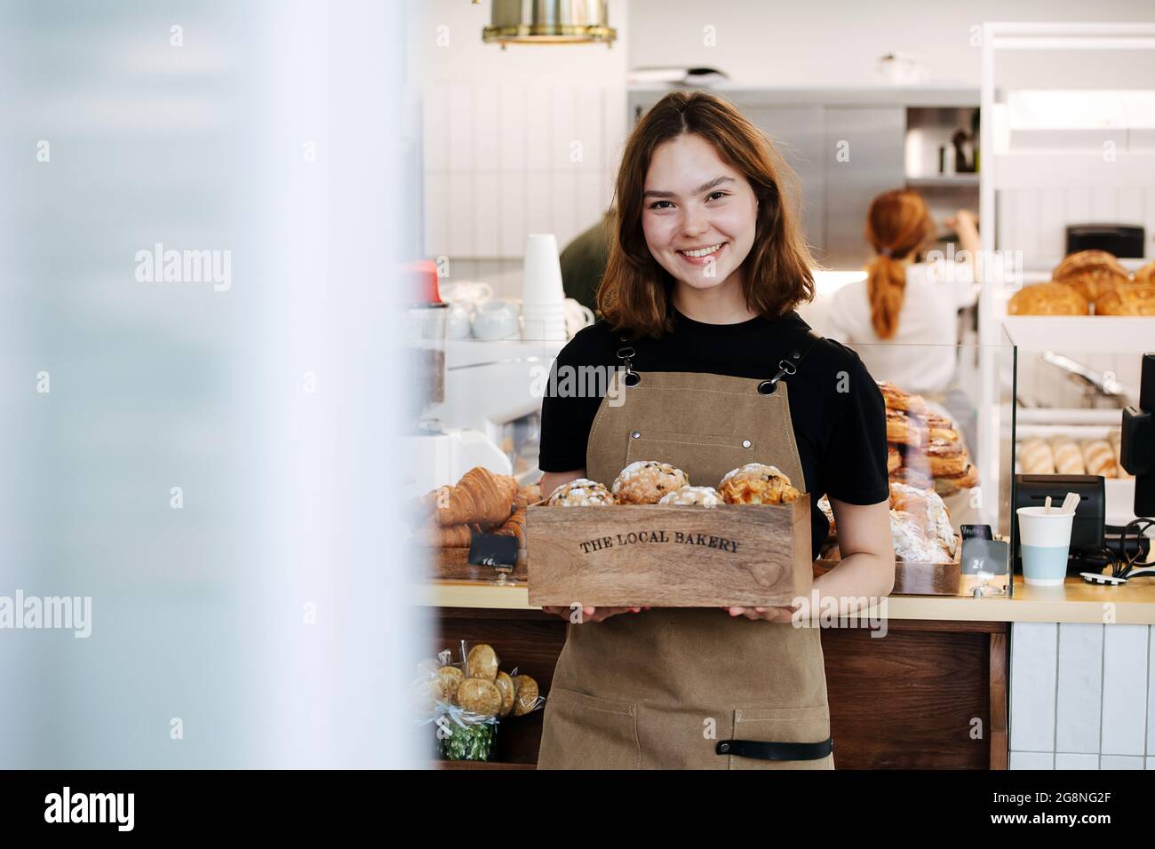 Friendly baker girl posing with a branded wooden box, filled with ...
