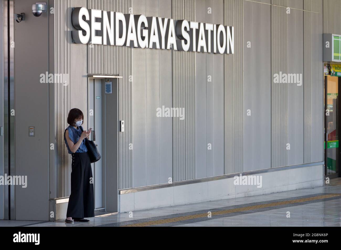 A woman wearing a surgical face mask uses her smart phone outside ...