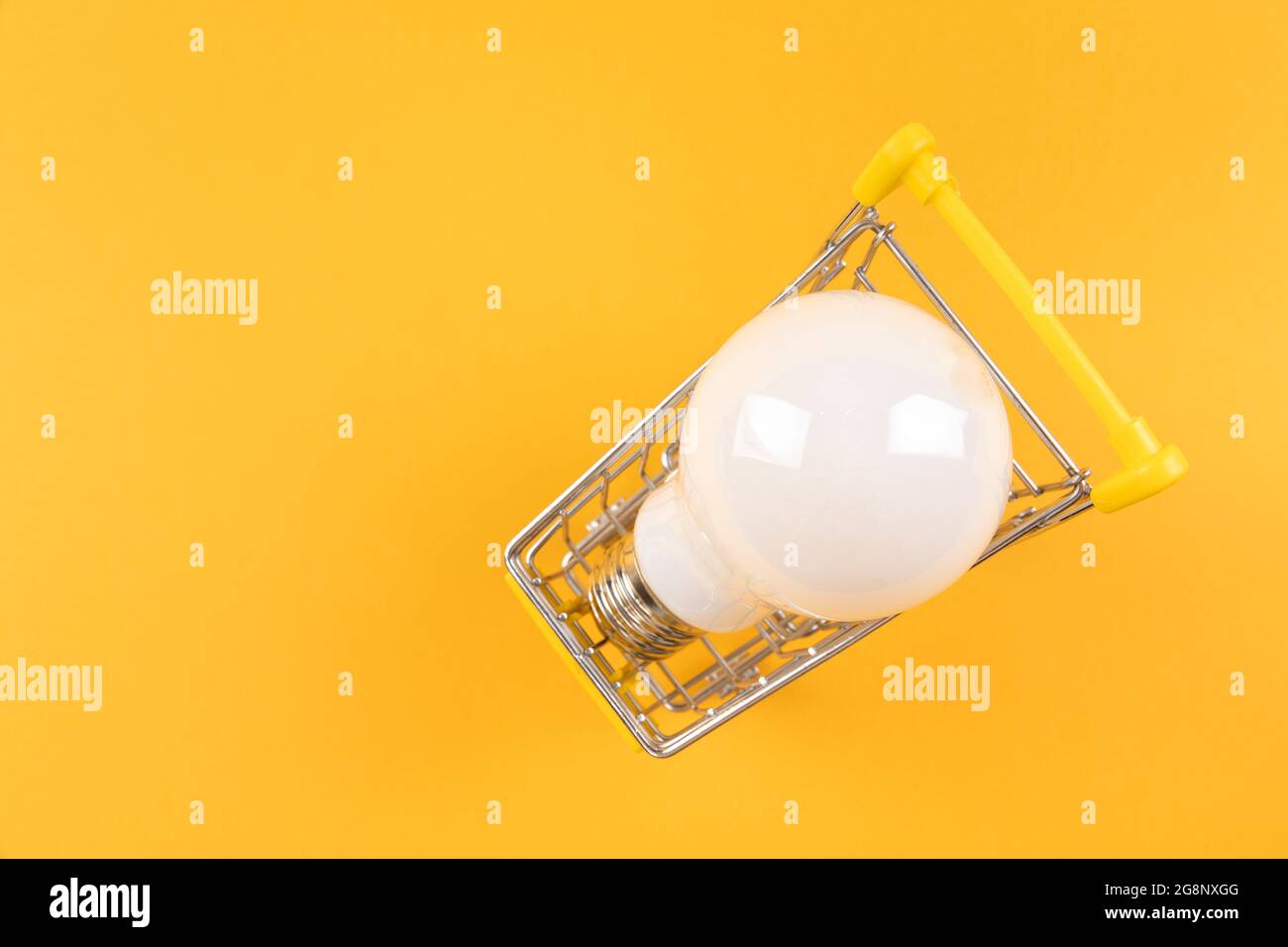 miniature shopping cart with opaque light bulb, yellow background, eco ...