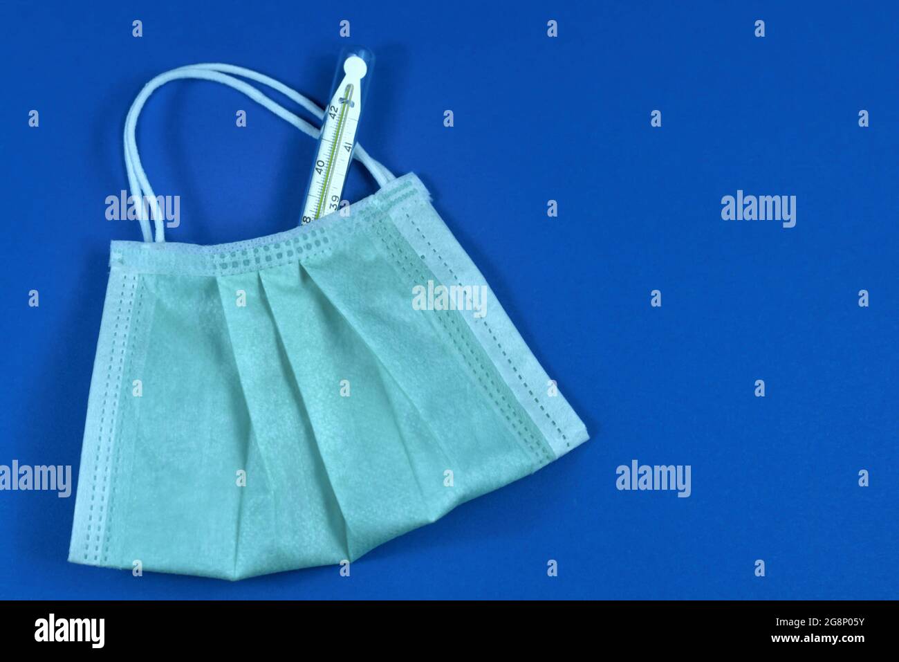 Medical thermometer and a face mask shape of bag on a blue background ...