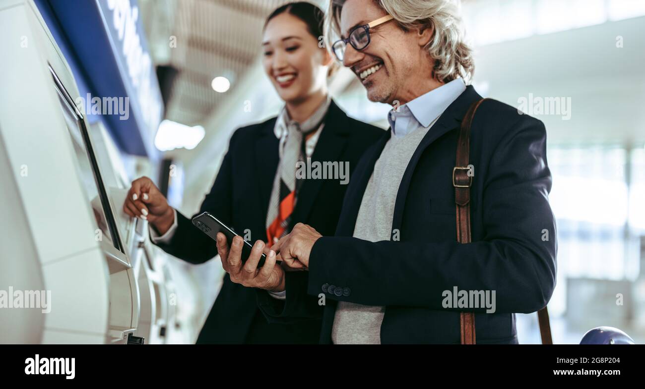 Happy businessman doing self check in on machine with flight attendant ...