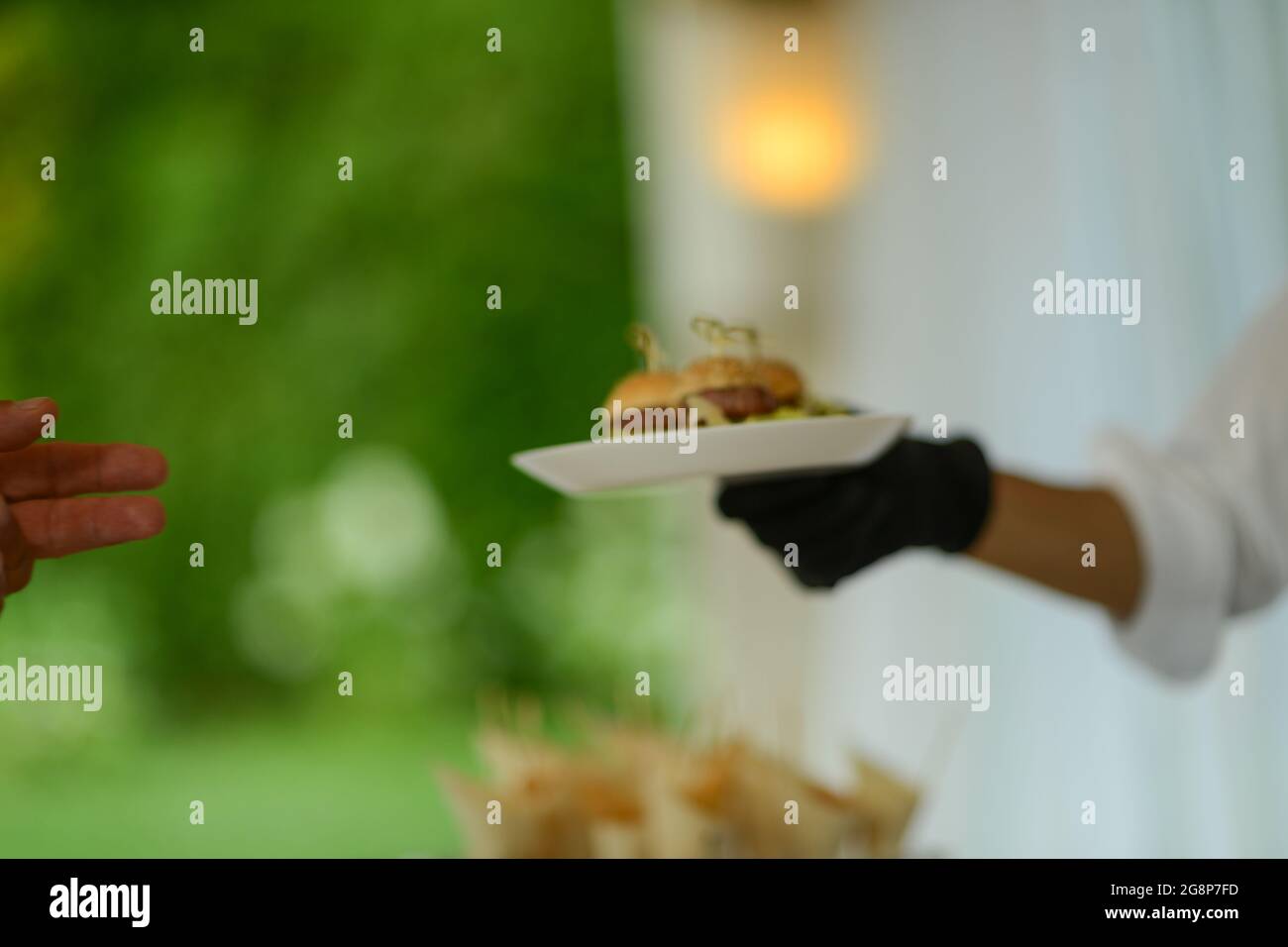 Chef handing out small burgers on a plate with a blurred green ...