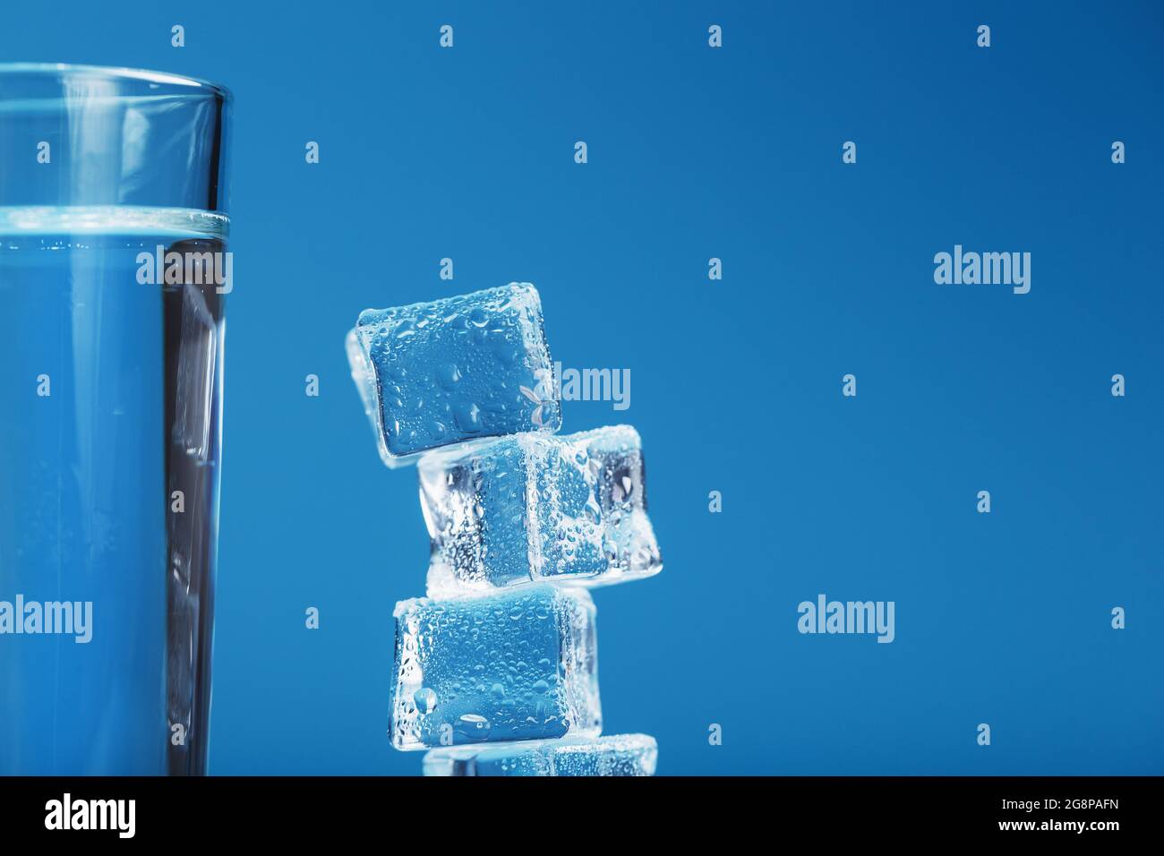 A glass of refreshing water and a tower of ice cubes on a blue ...