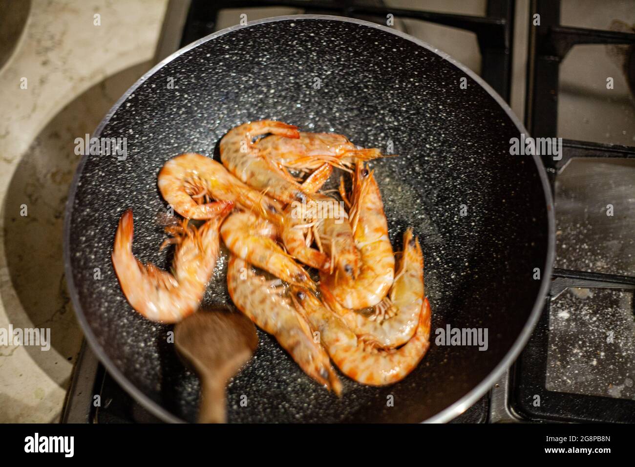Wooden spoon to turn the wild Mediterranean prawns in a black frying ...
