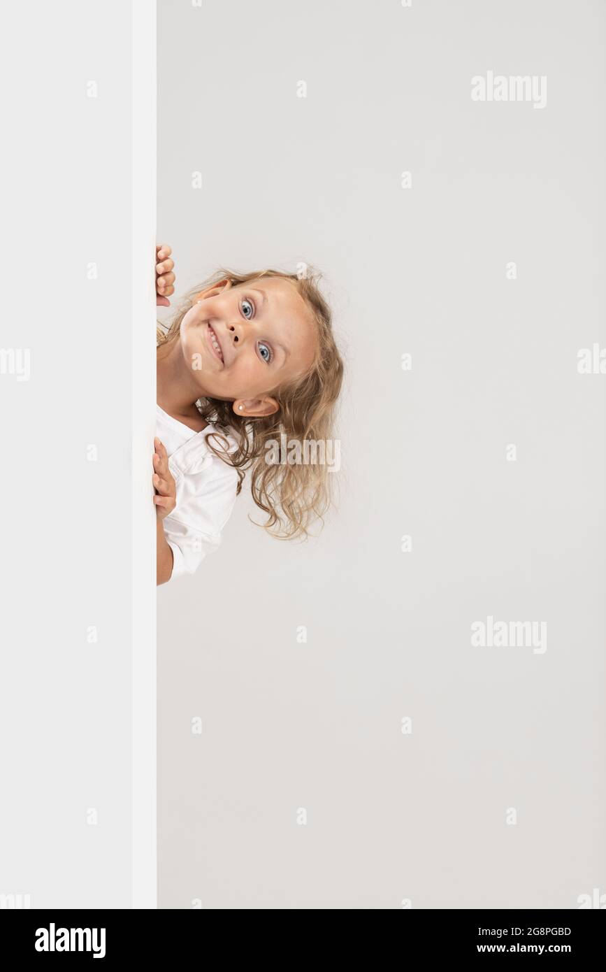 Portrait of little cute smiling Caucasian girl peeking around the ...