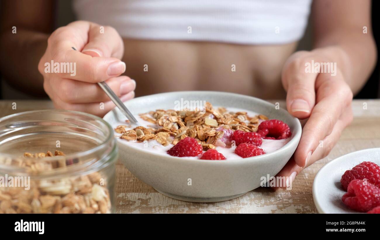 Young fitness woman eating granola bowl with raspberries for breakfast ...