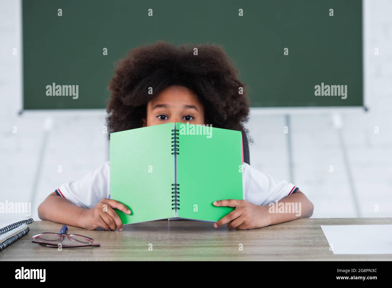 African american kid covering face with book in classroom Stock Photo ...