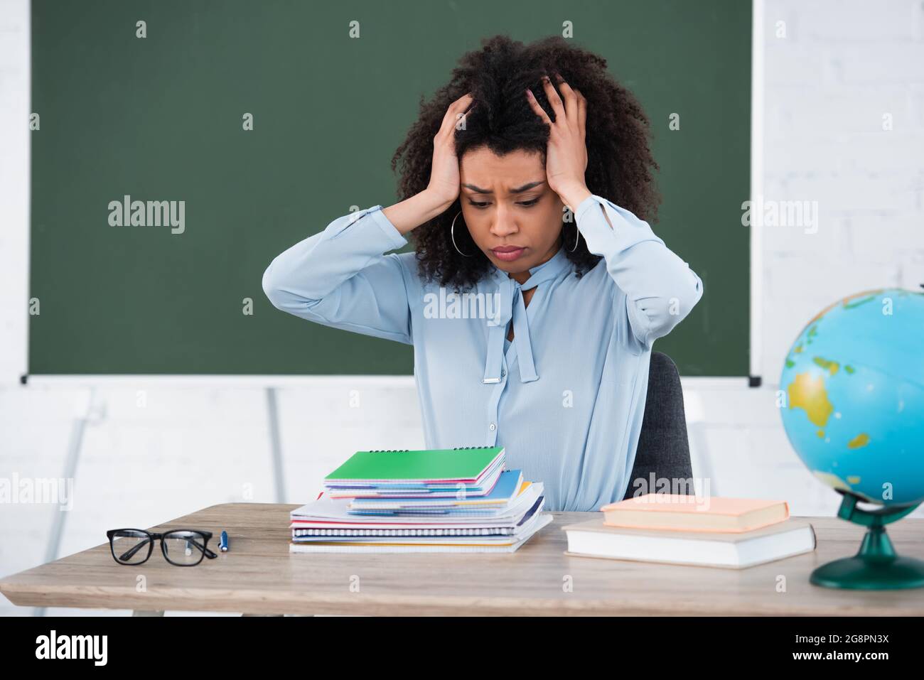 Tired african american teacher having headache near stationery and ...