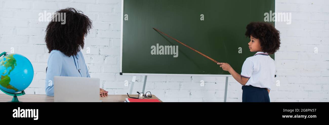 African american pupil pointing at chalkboard near teacher in classroom ...