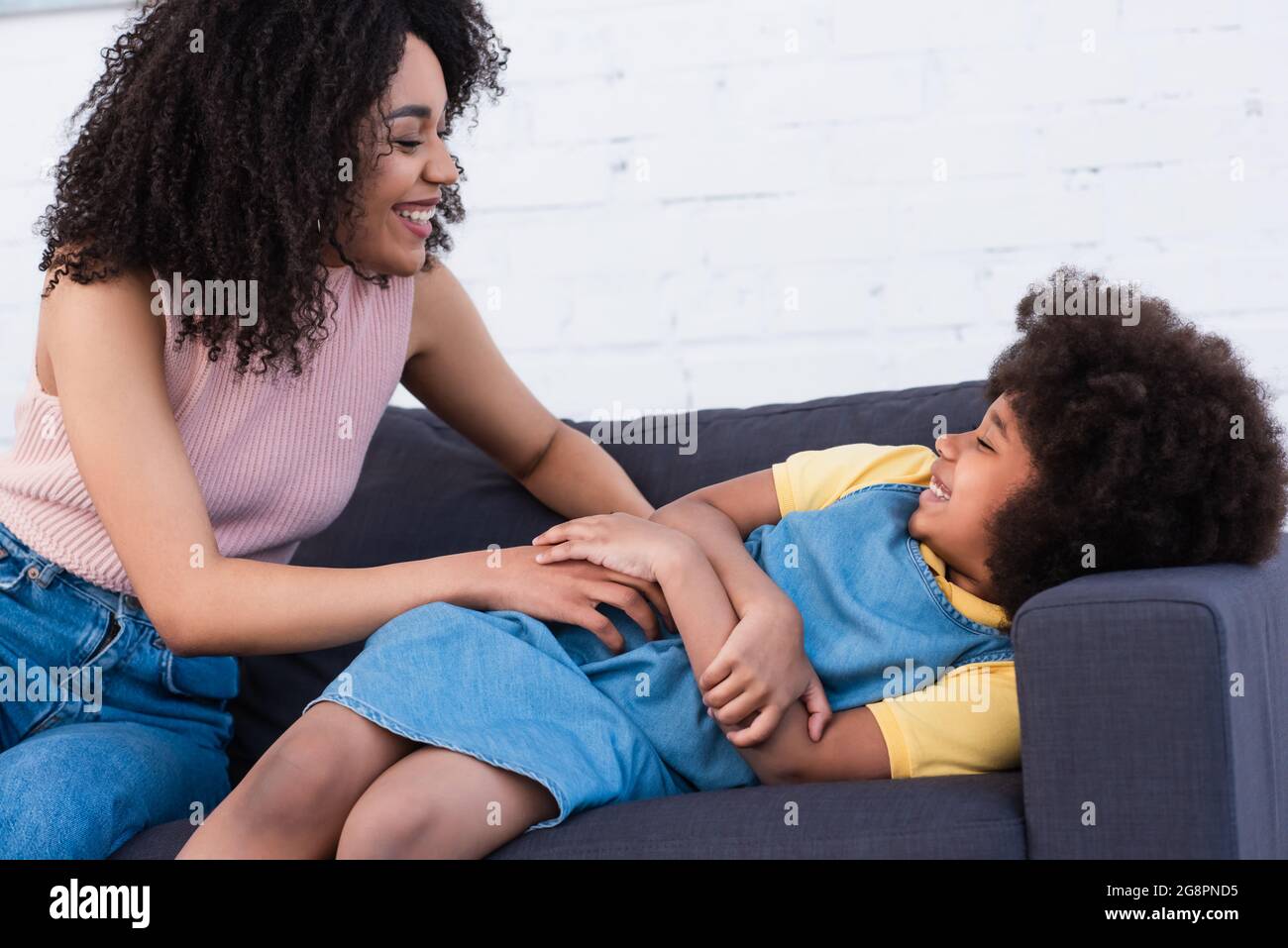 Cheerful african american woman tickling daughter on couch Stock Photo - Alamy