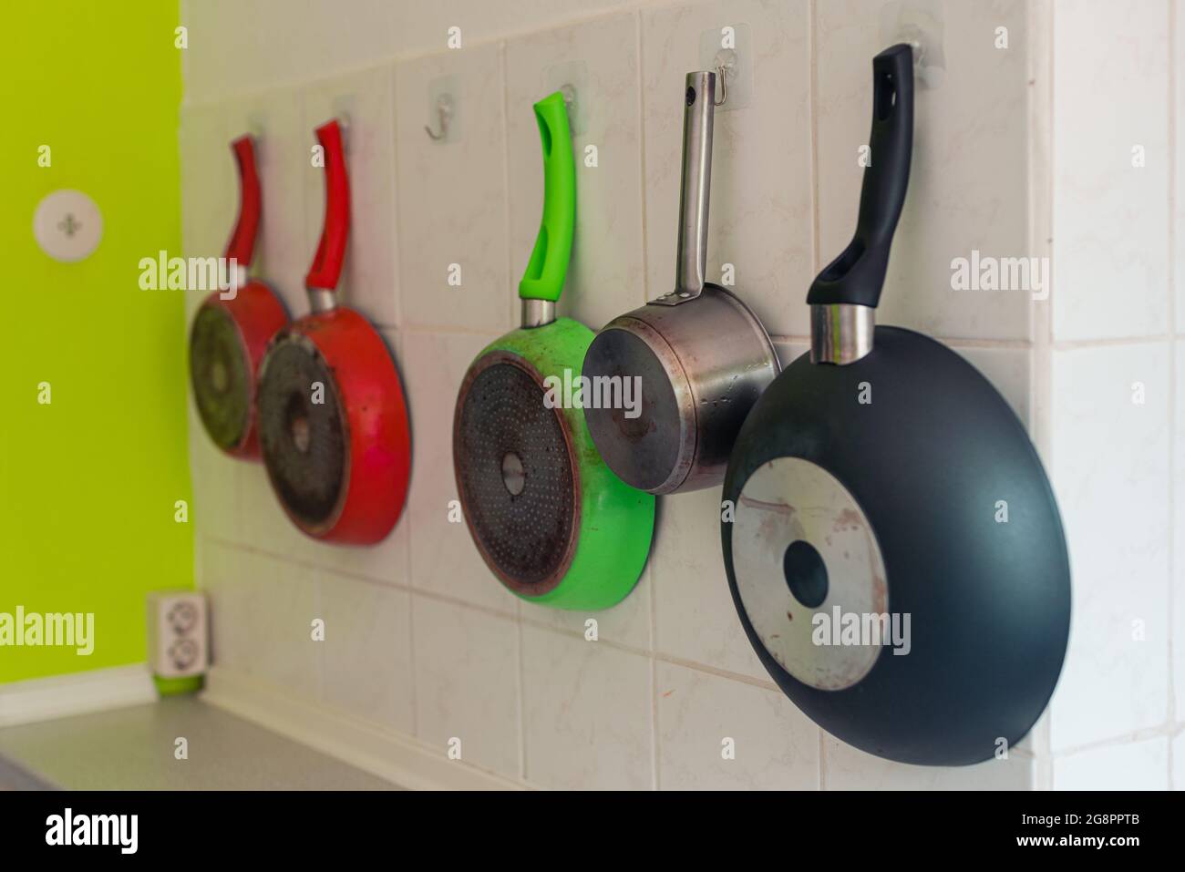 Closeup shot of frying pans of different colors hung on kitchen wall ...
