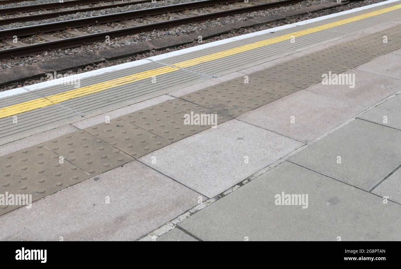 Train platform showing yellow safety line on paving and railway tracks ...