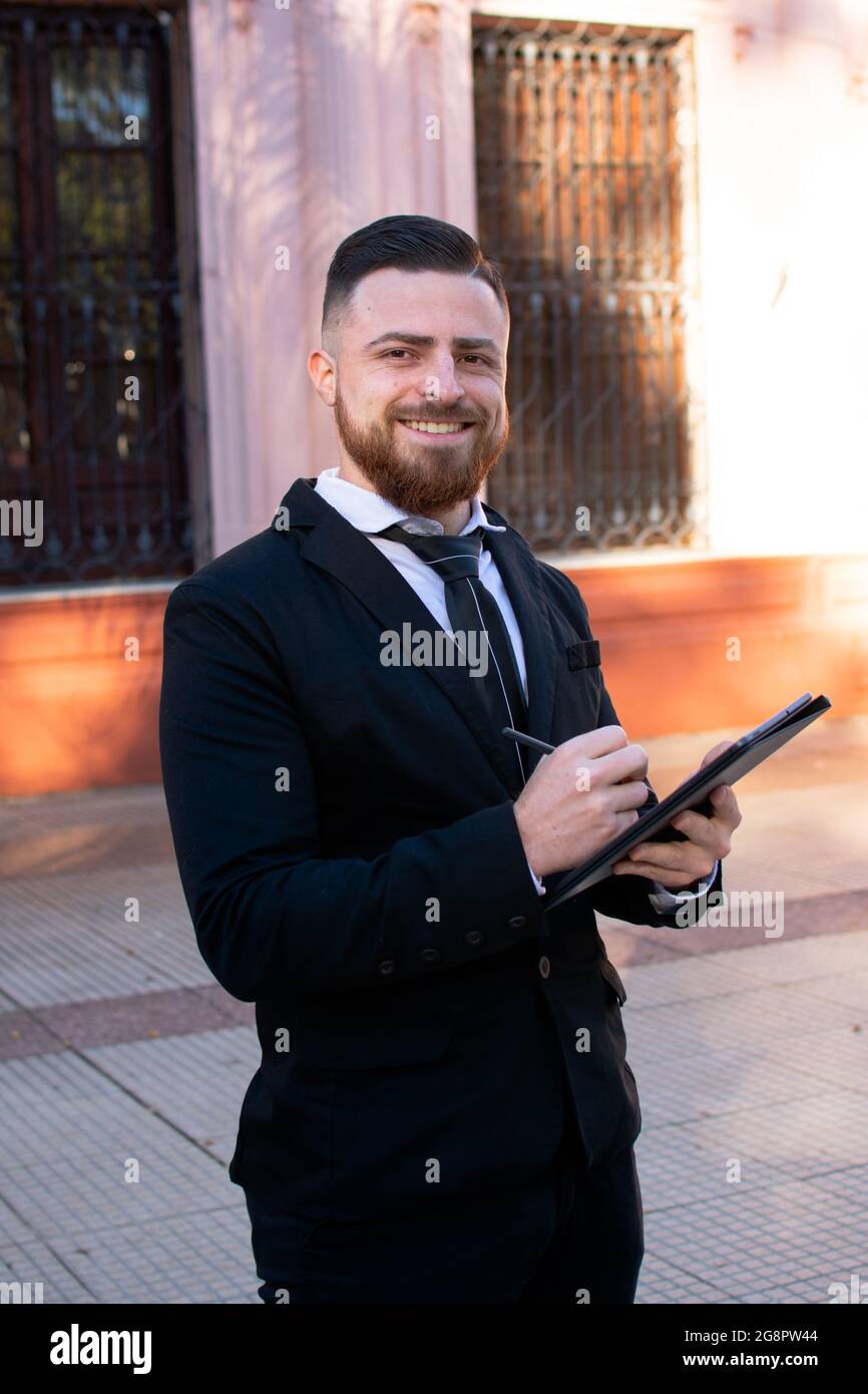 Happy Hispanic male in an elegant suit doing some notes in the tablet ...