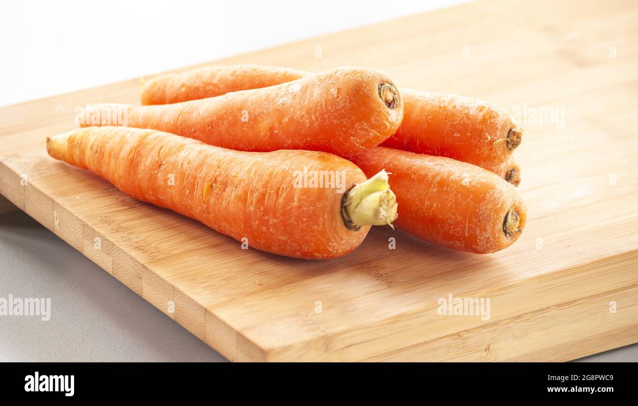 Closeup of freshly picked long carrots on a sharp wooden cutting board ...