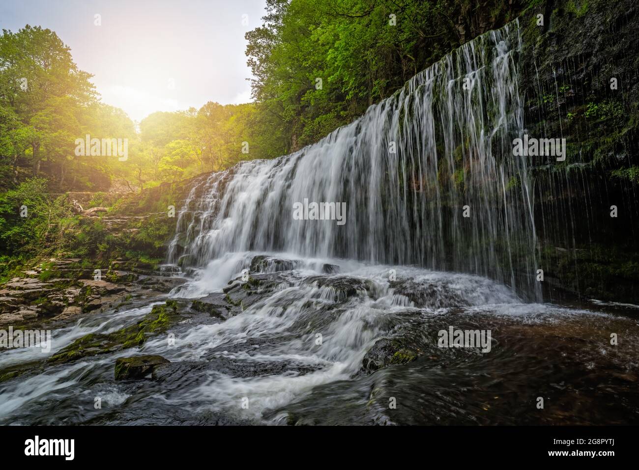 A waterfall surrounded by moss, trees, and stones in Ystradfellte Neath ...