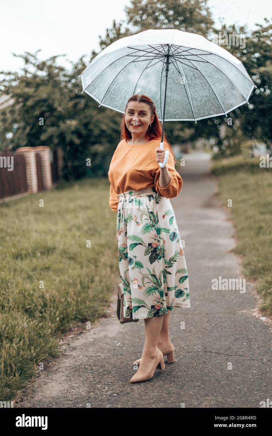 Cheerful young woman in bright clothes under a transparent umbrella in ...