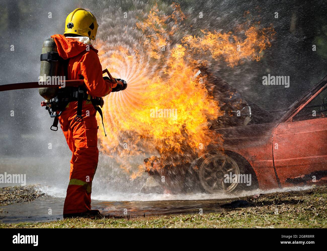 Fire fighter hosing water to extinguish a fire over the car in accident ...