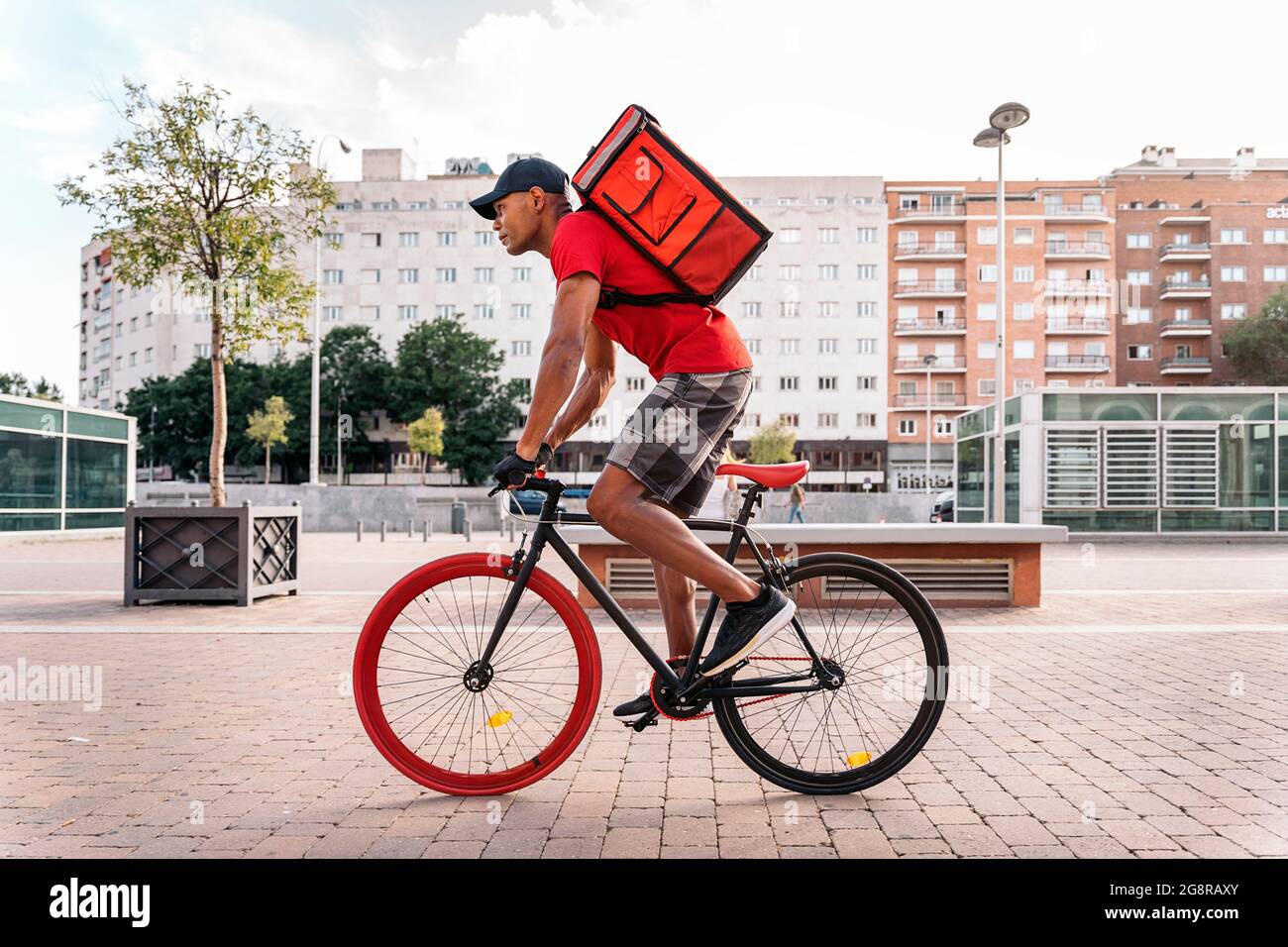 African delivery man wearing cap riding his bike in the city in his way ...