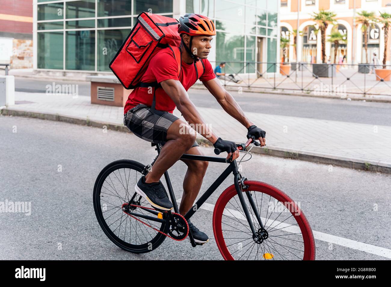 African delivery man wearing safety helmet riding his bike in the city ...