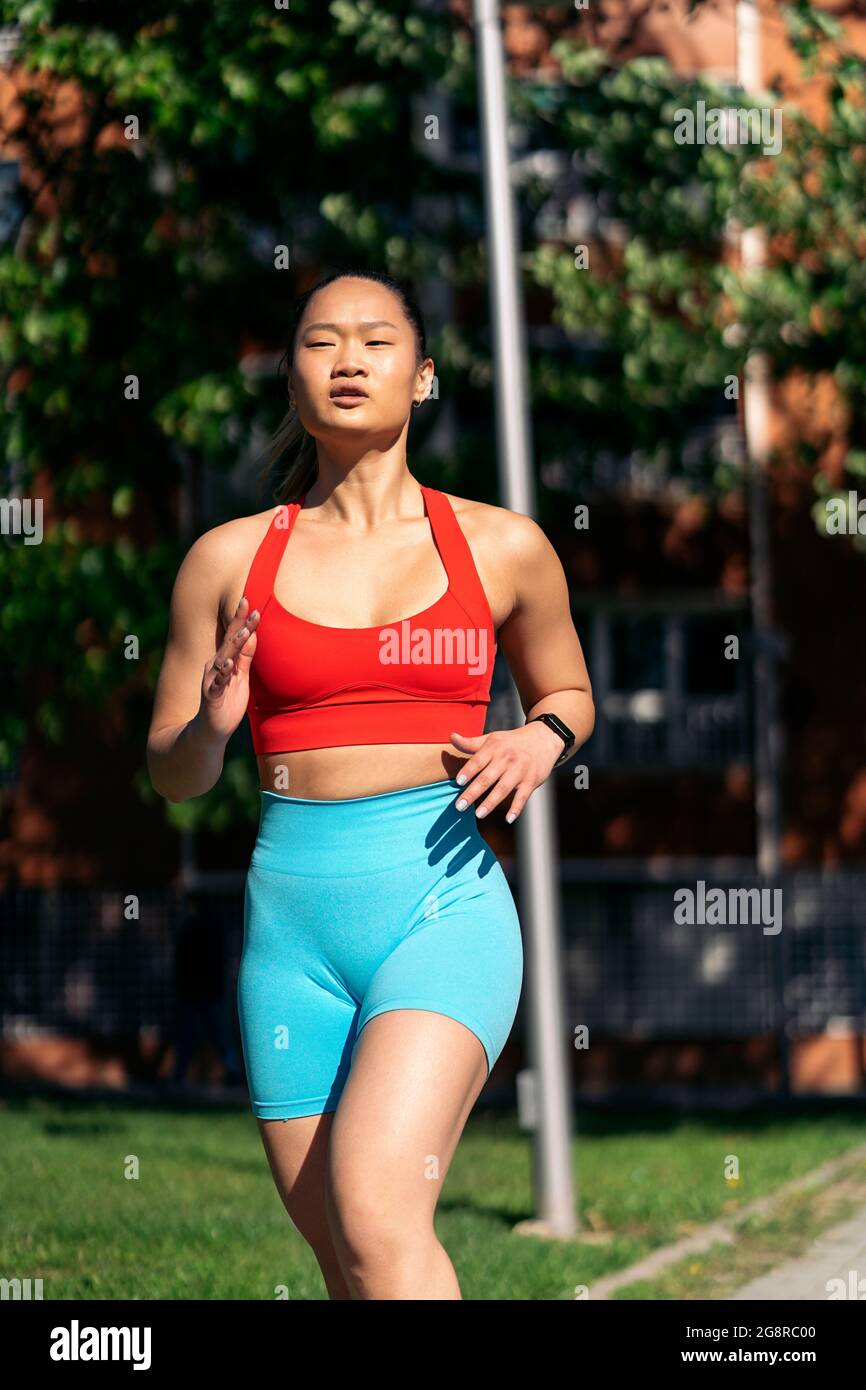 Active asian woman with sports clothes running in the park during sunny ...