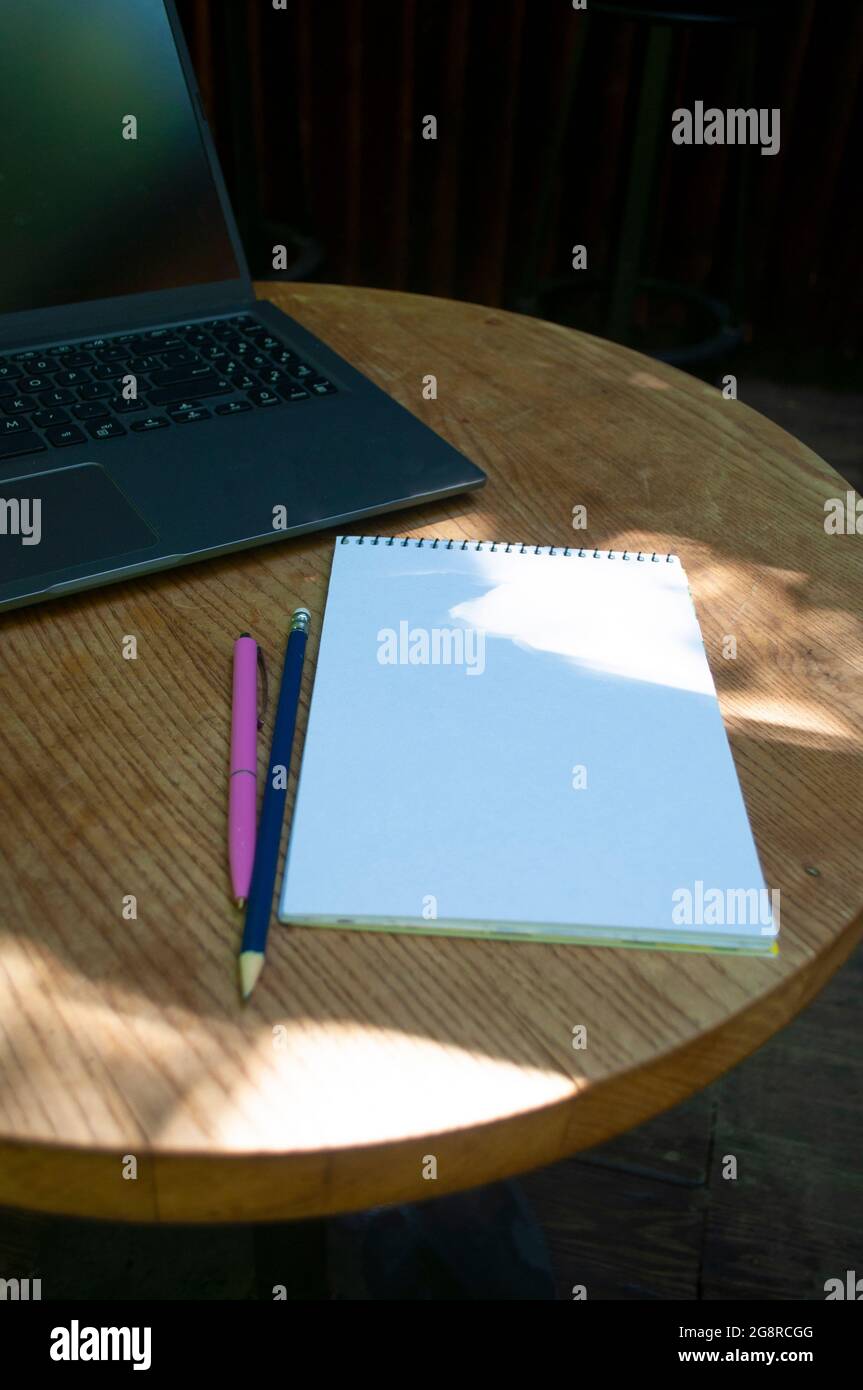 A laptop, notepad, a pencil and a pen on a wooden round shape table ...