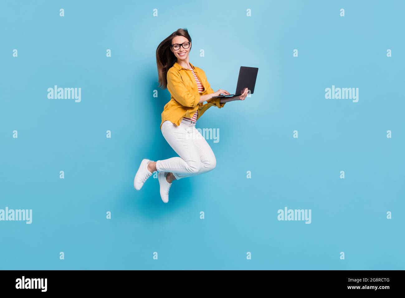 Full size photo of charming happy young woman jump up hold computer ...