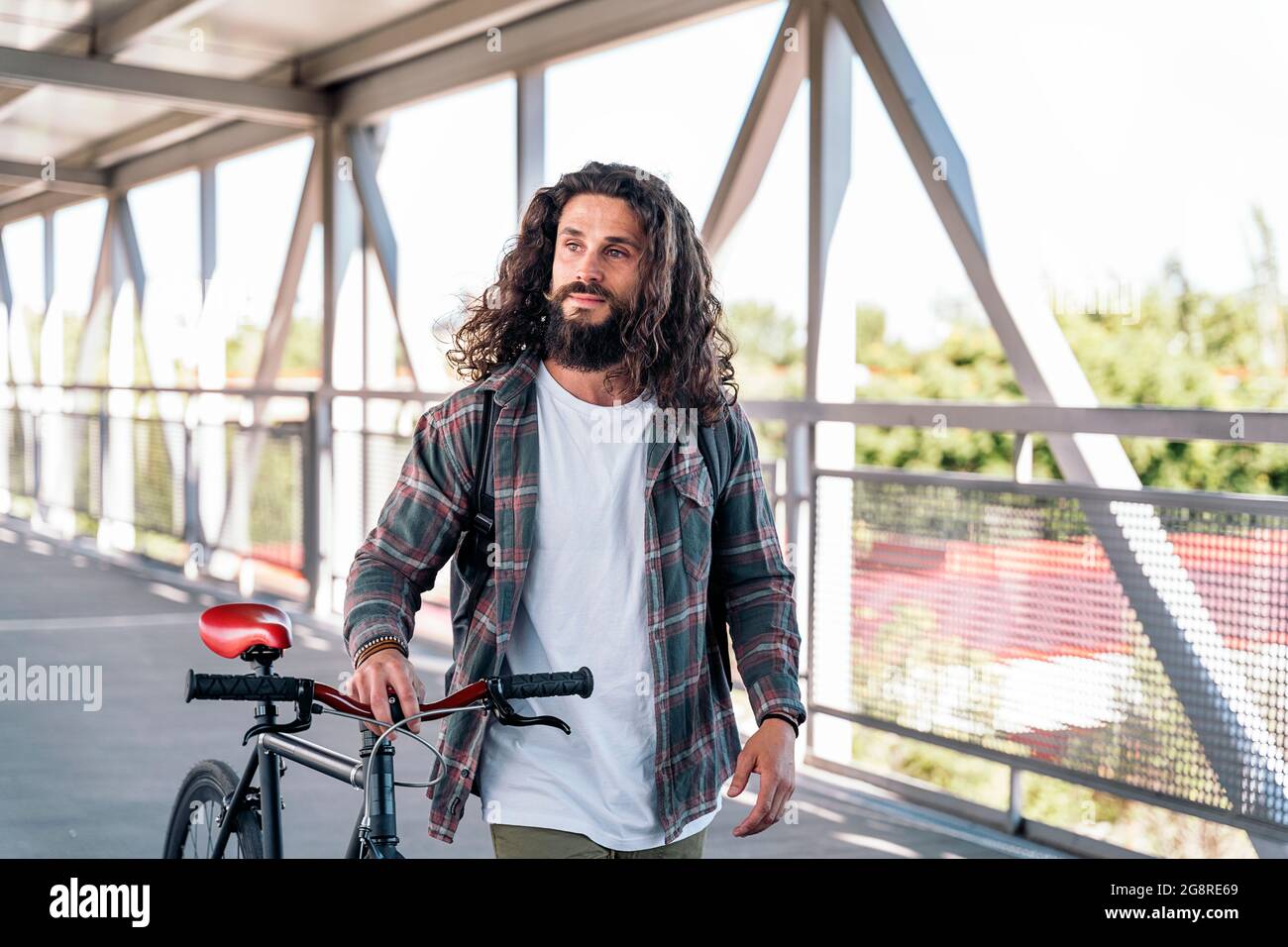 Cool bearded man with long hair smiling and looking to the side while holding his bike Stock ...